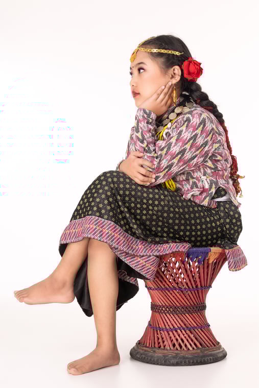 A charming traditional little girl is sitting on a muda and is lost in ...