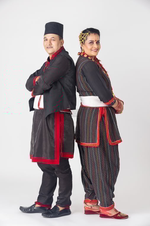 A Newari couple posing back-to-back while smiling and folding their ...